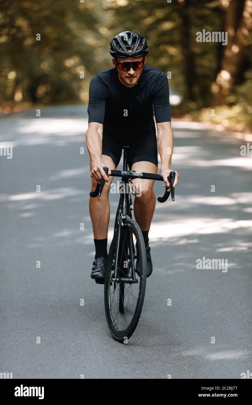 Front view of strong male cyclist in sportswear riding black bike with ...