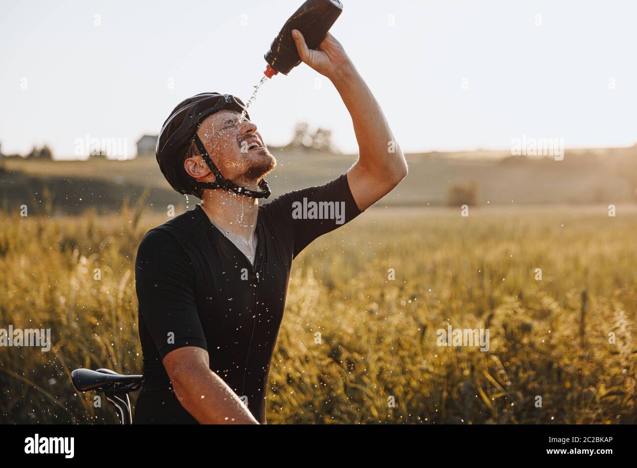 Mature tired athlete in sportswear and protective helmet splashing cold ...