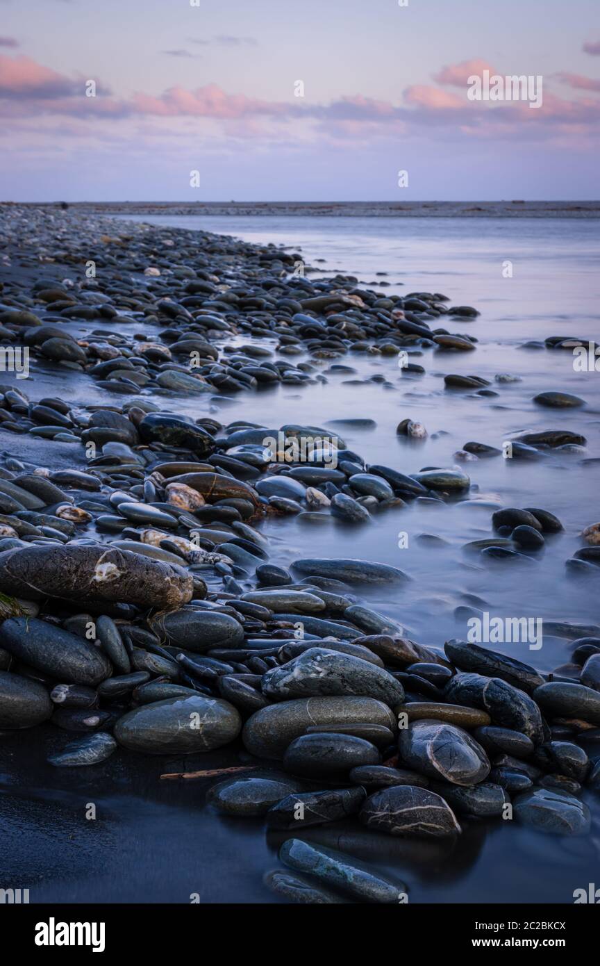 Early morning light over wet pebbles at Okarito on the west coast of ...