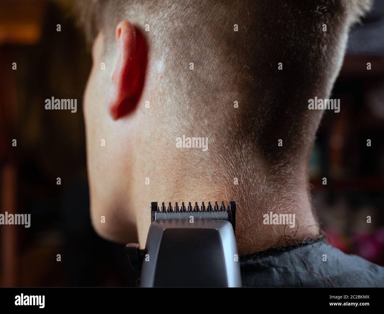 Male hairstylist serving client, making haircut using trimming machine ...