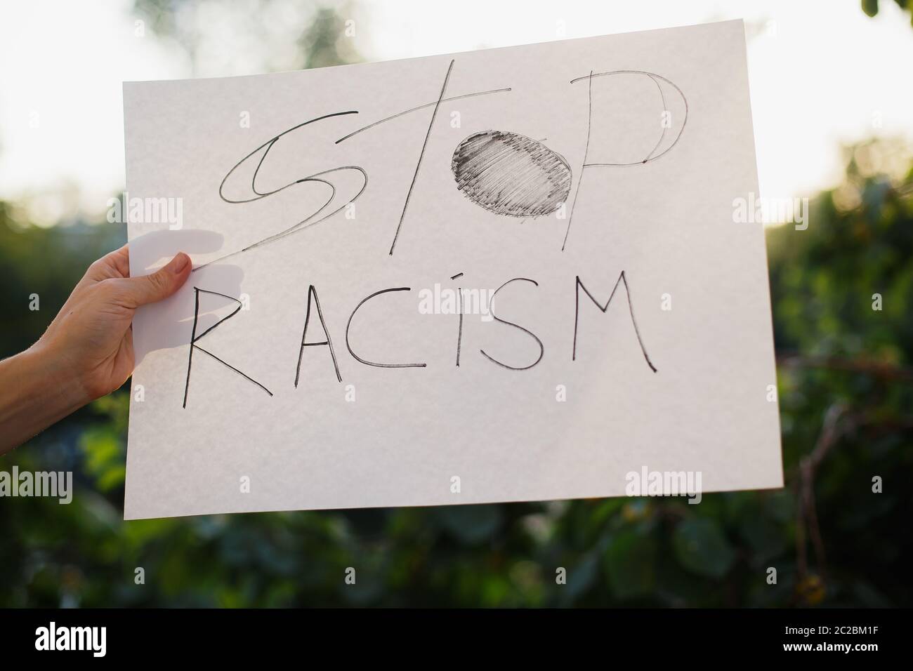 Woman holding white paper with text "Stop racism". Against the ...