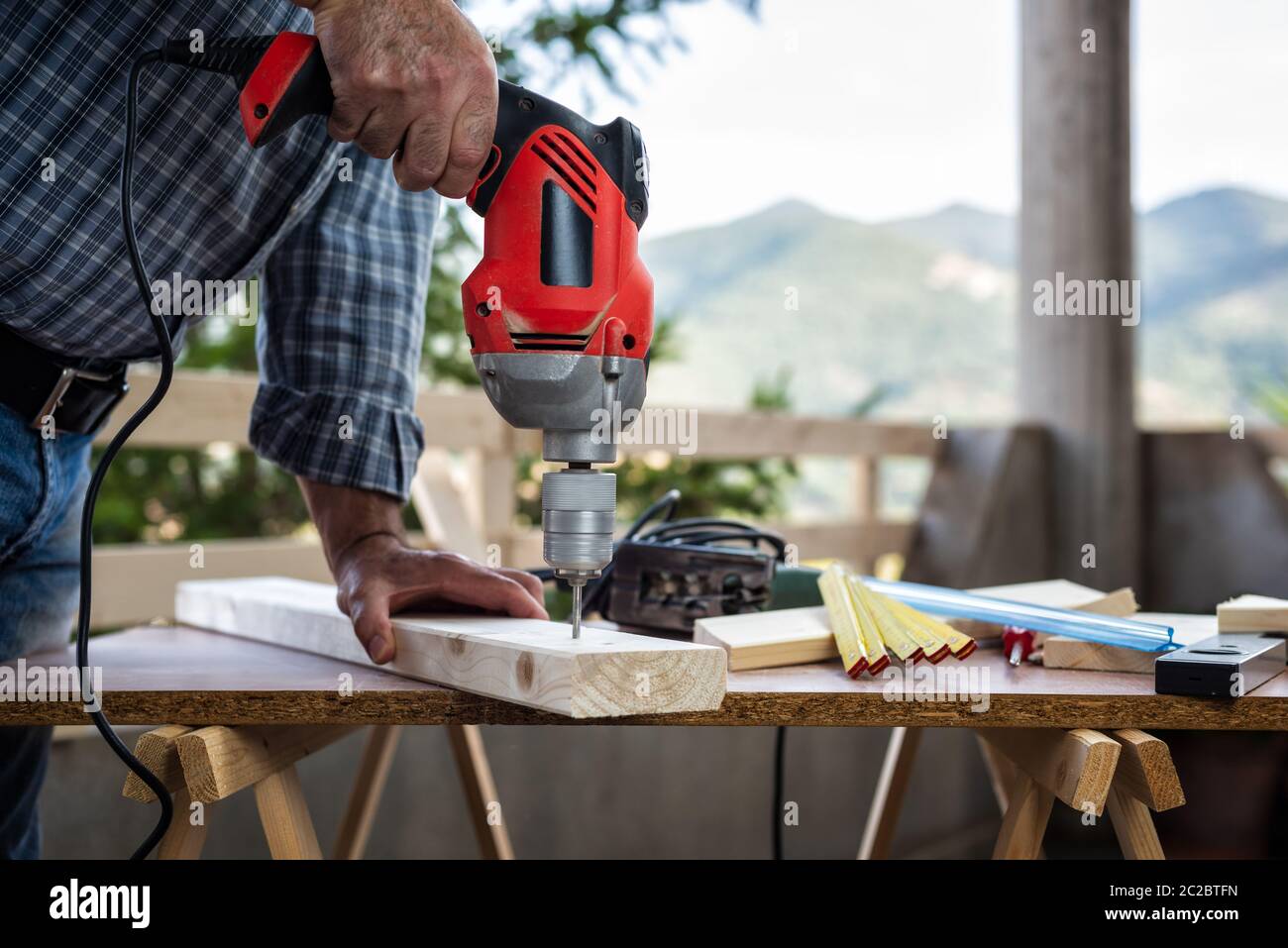 Adult craftsman carpenter with electric drill works makes a hole on a ...