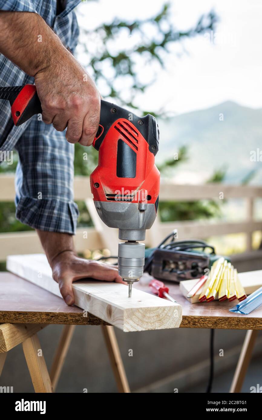 Adult craftsman carpenter with electric drill works makes a hole on a ...