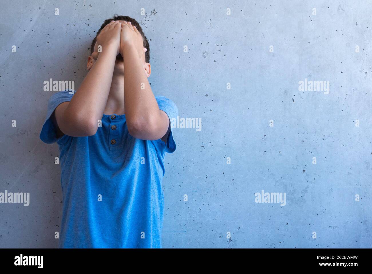 Upset sad boy stand alone and leaning on gray wall. Learning ...