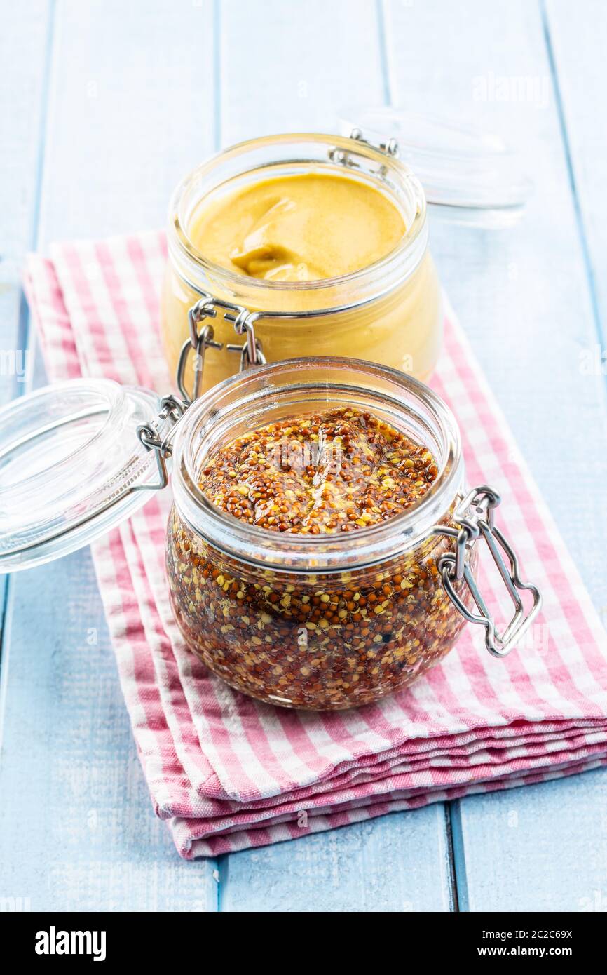 Yellow mustard and whole grain mustard in jar on blue table Stock Photo ...