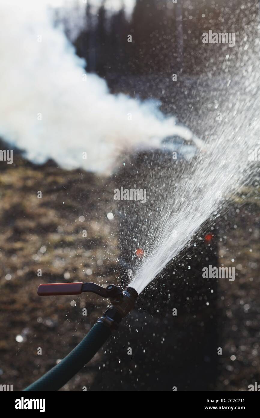 Water spraying from water hose near fire burning in old rusty barrel ...