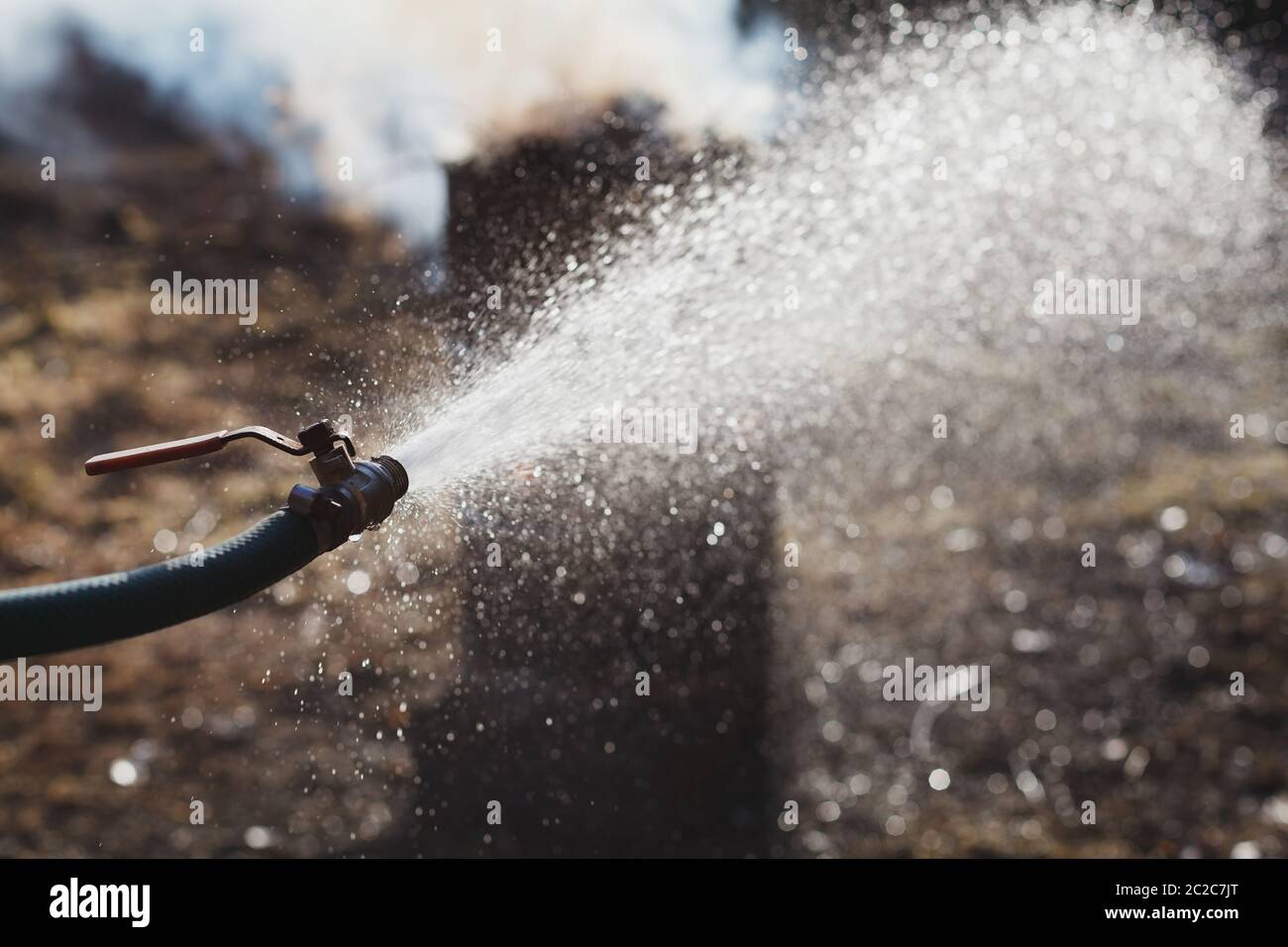 Water spraying from water hose near fire burning in old rusty barrel ...