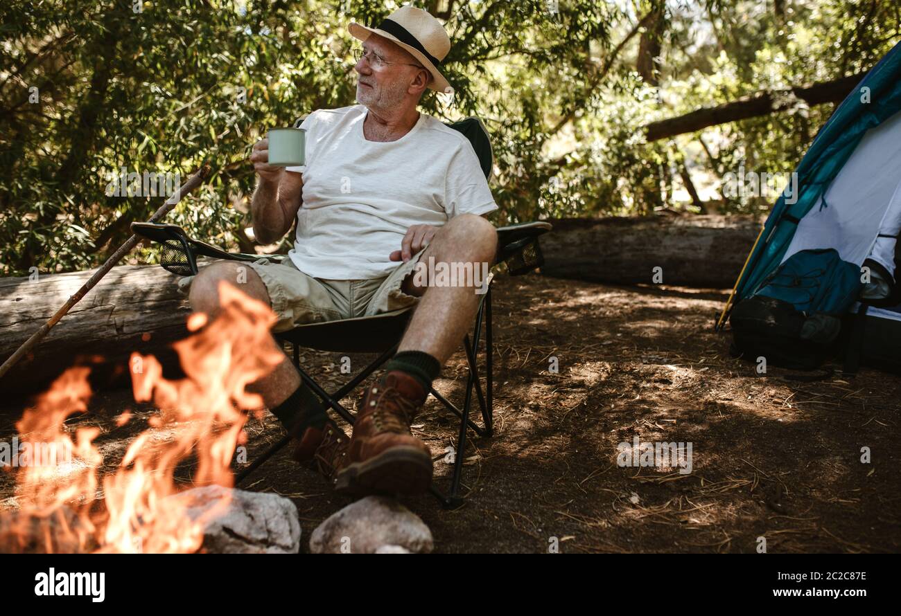 Retired man sitting near campfire and having coffee. Senior male ...