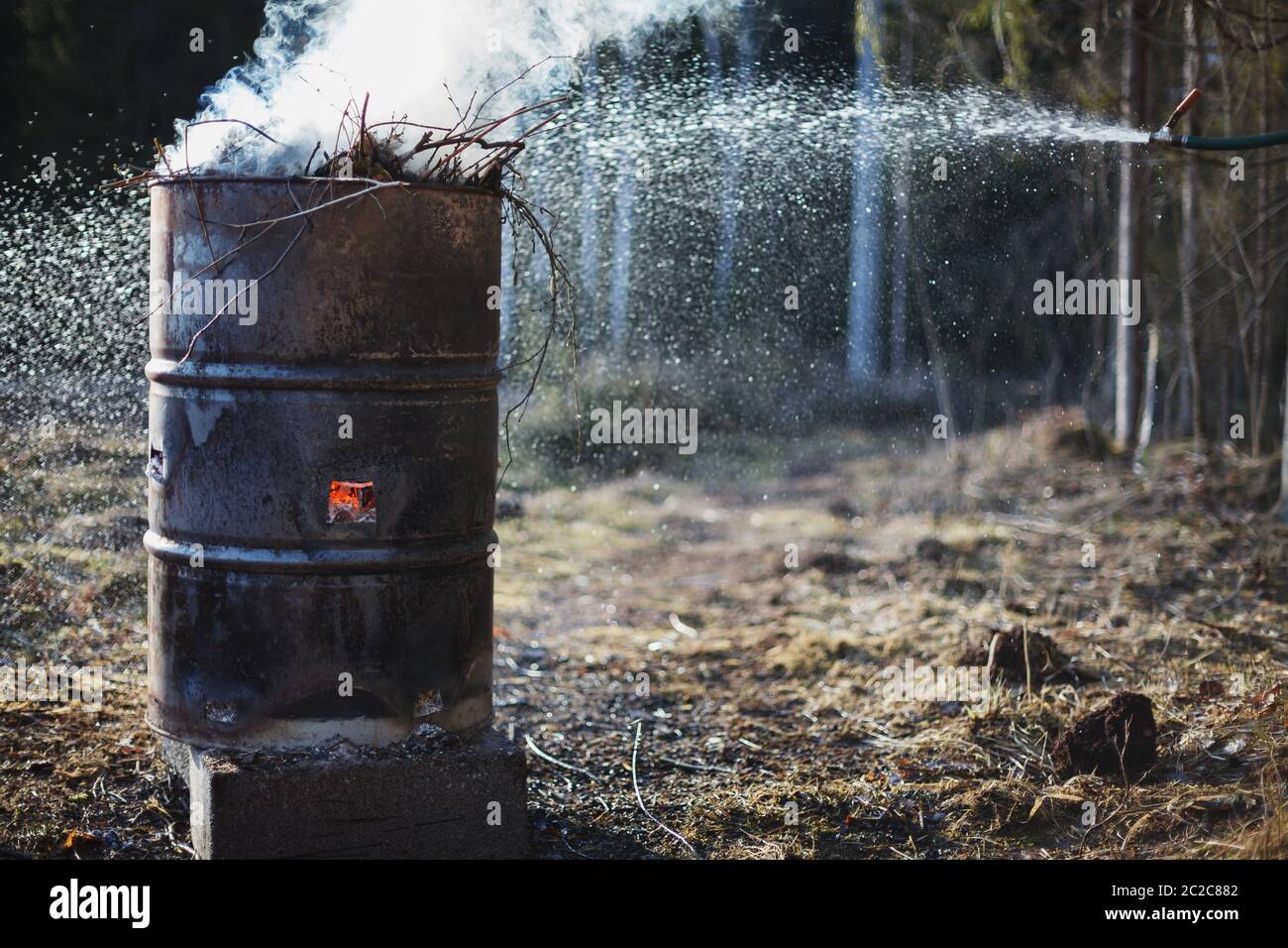 Water spraying from water hose near fire burning in old rusty barrel ...