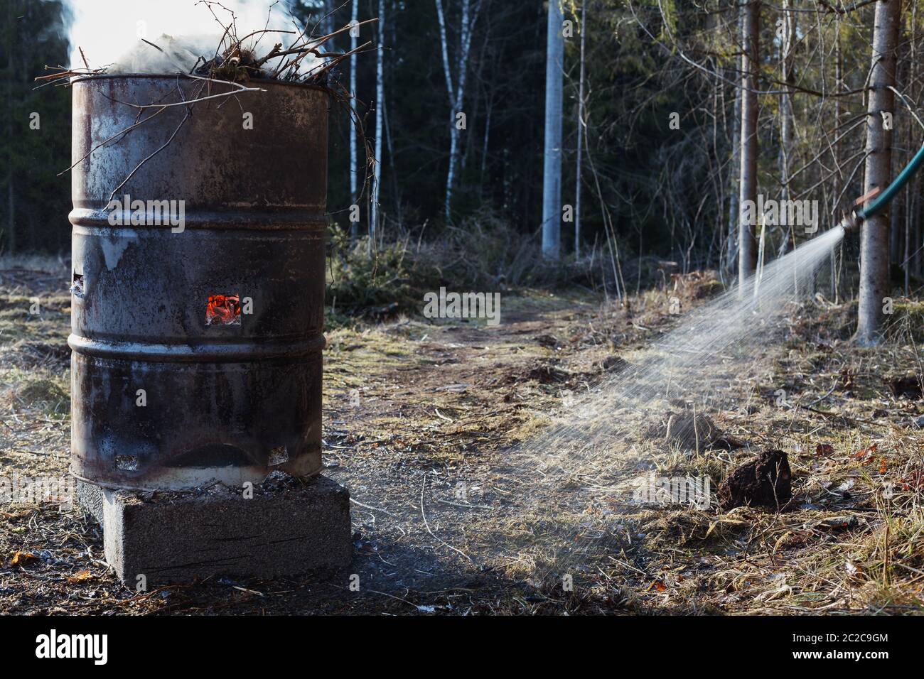 Water spraying from water hose near fire burning in old rusty barrel ...