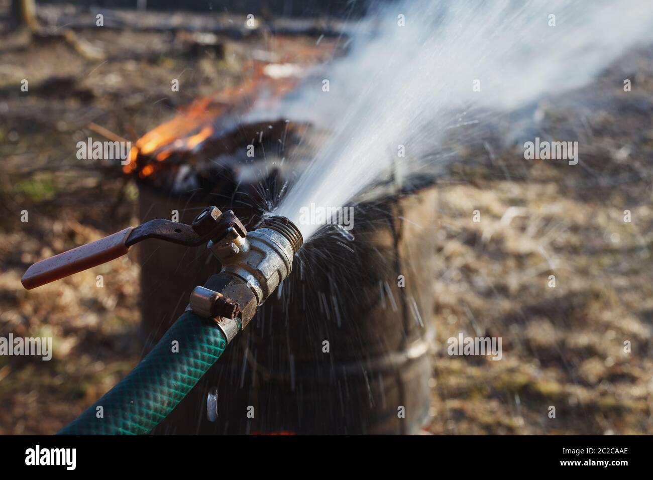 Water spraying from water hose near fire burning in old rusty barrel ...