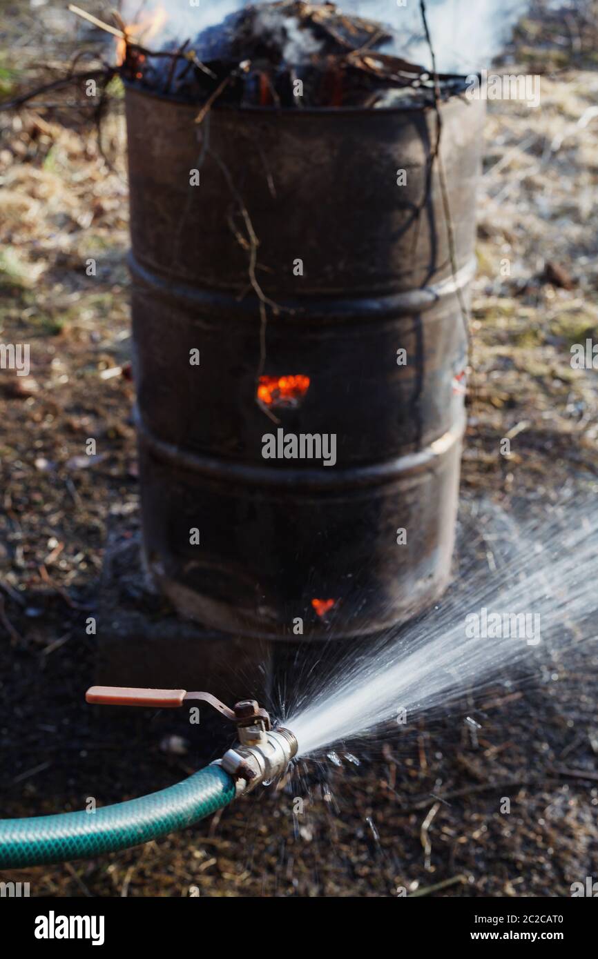Water spraying from water hose near fire burning in old rusty barrel ...