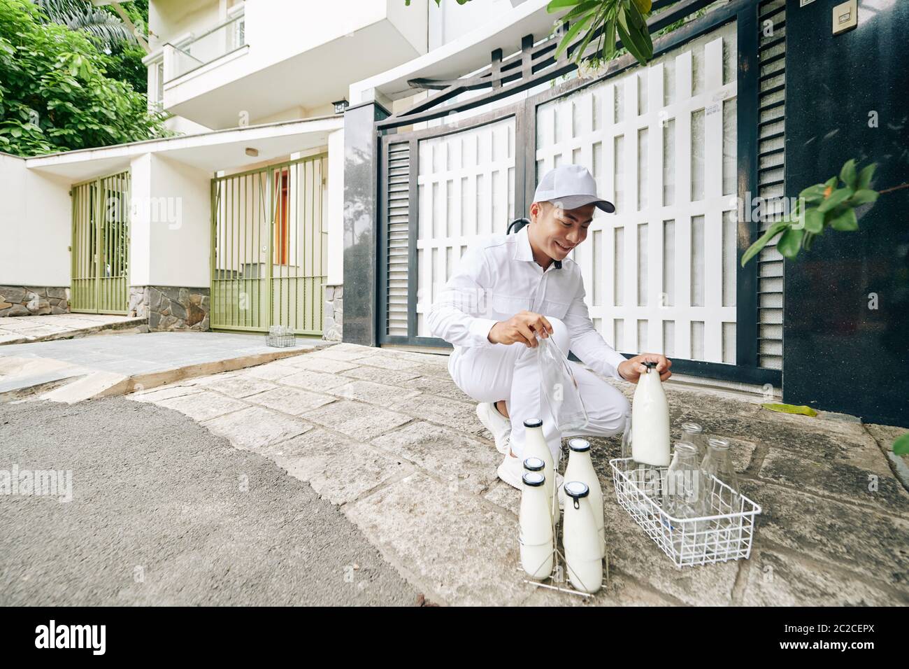 Joyful Asian milkman wearing perfect white uniform delivering milk and ...