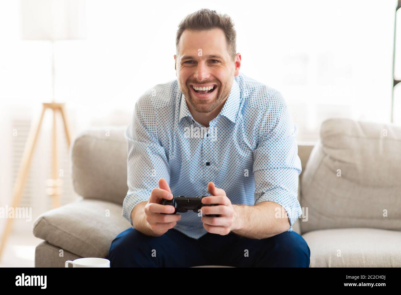Young man sitting on couch playing video games Stock Photo - Alamy