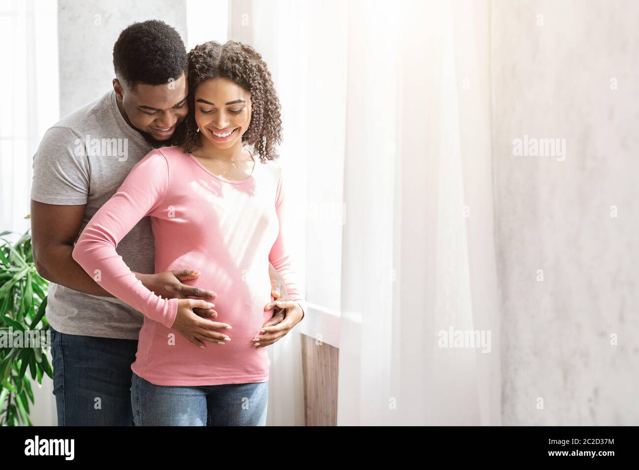 Happy expecting family standing next to window, touching belly Stock ...