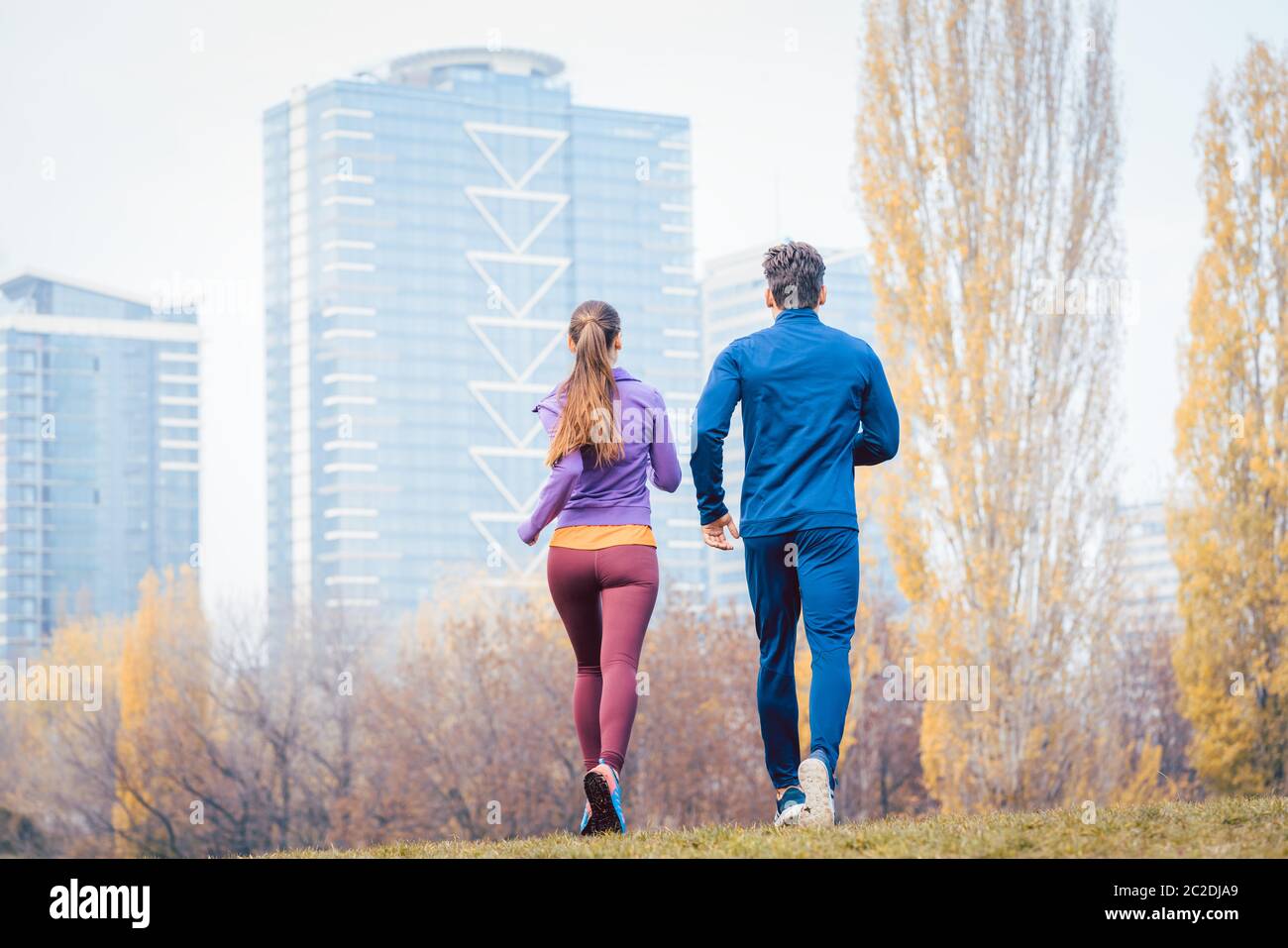 Couple seen from behind running thru a city in fall with colorful ...
