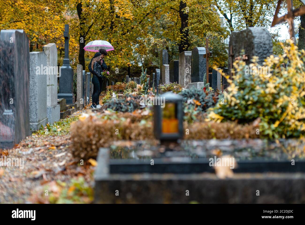 Graves on cemetery in autumn with a couple mourning the dead standing ...