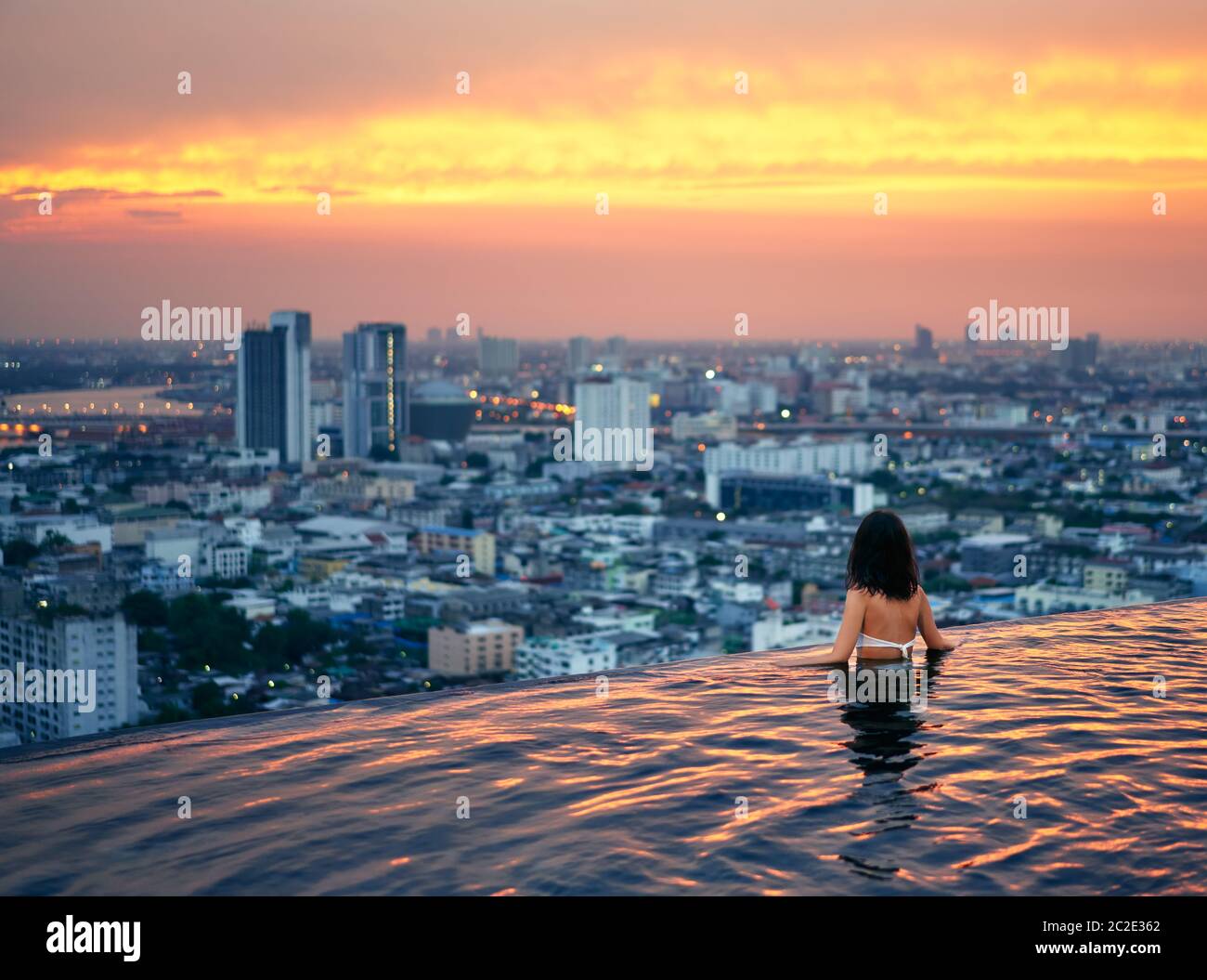 Young woman relax in swimming pool on roof top during amazing sunset ...