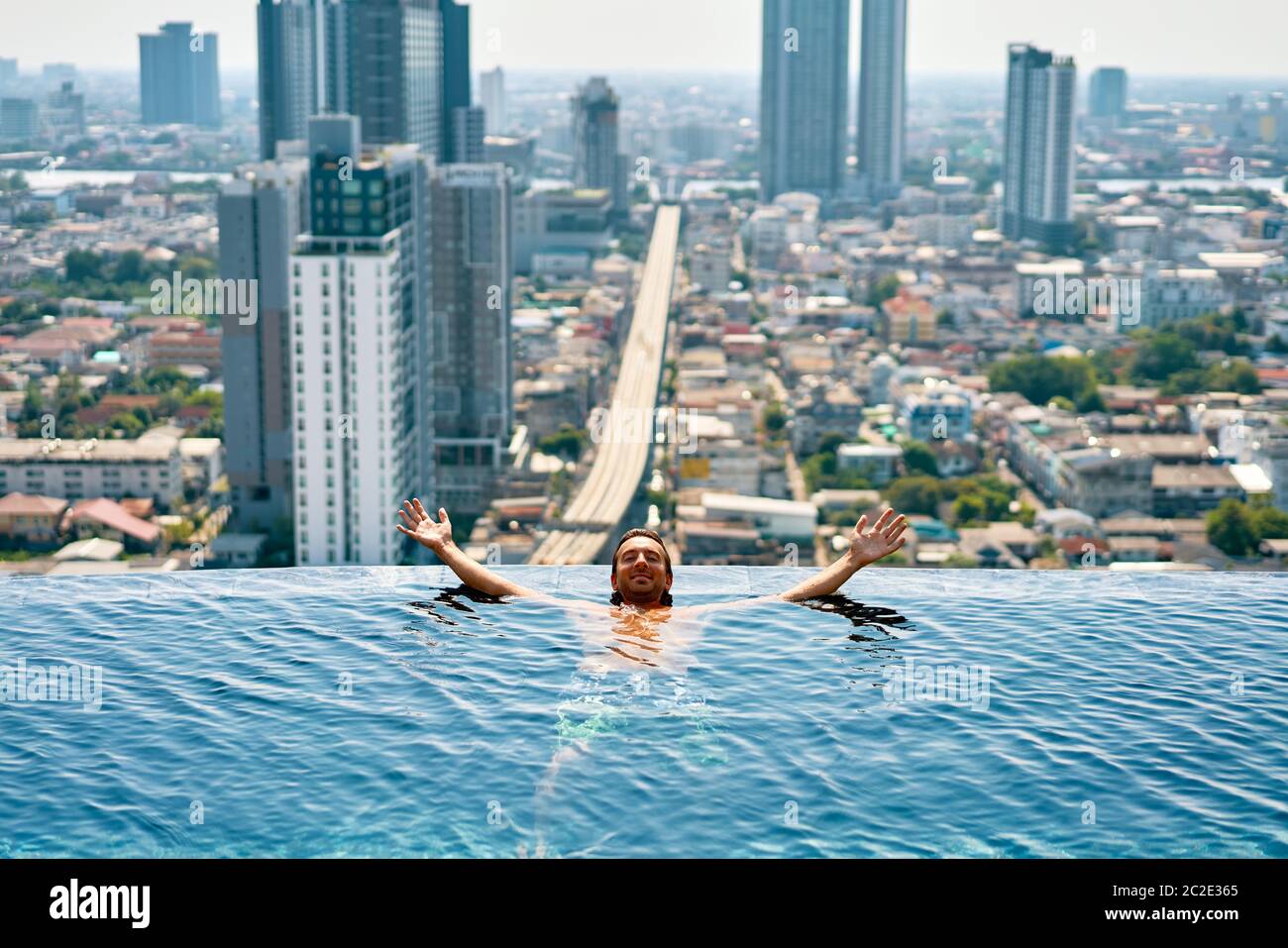 Young happy man relax on the edge of swimming pool in roof top of hotel ...