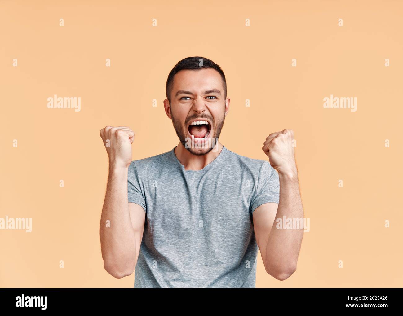 Happy man celebrating his success with winner gesture on beige ...