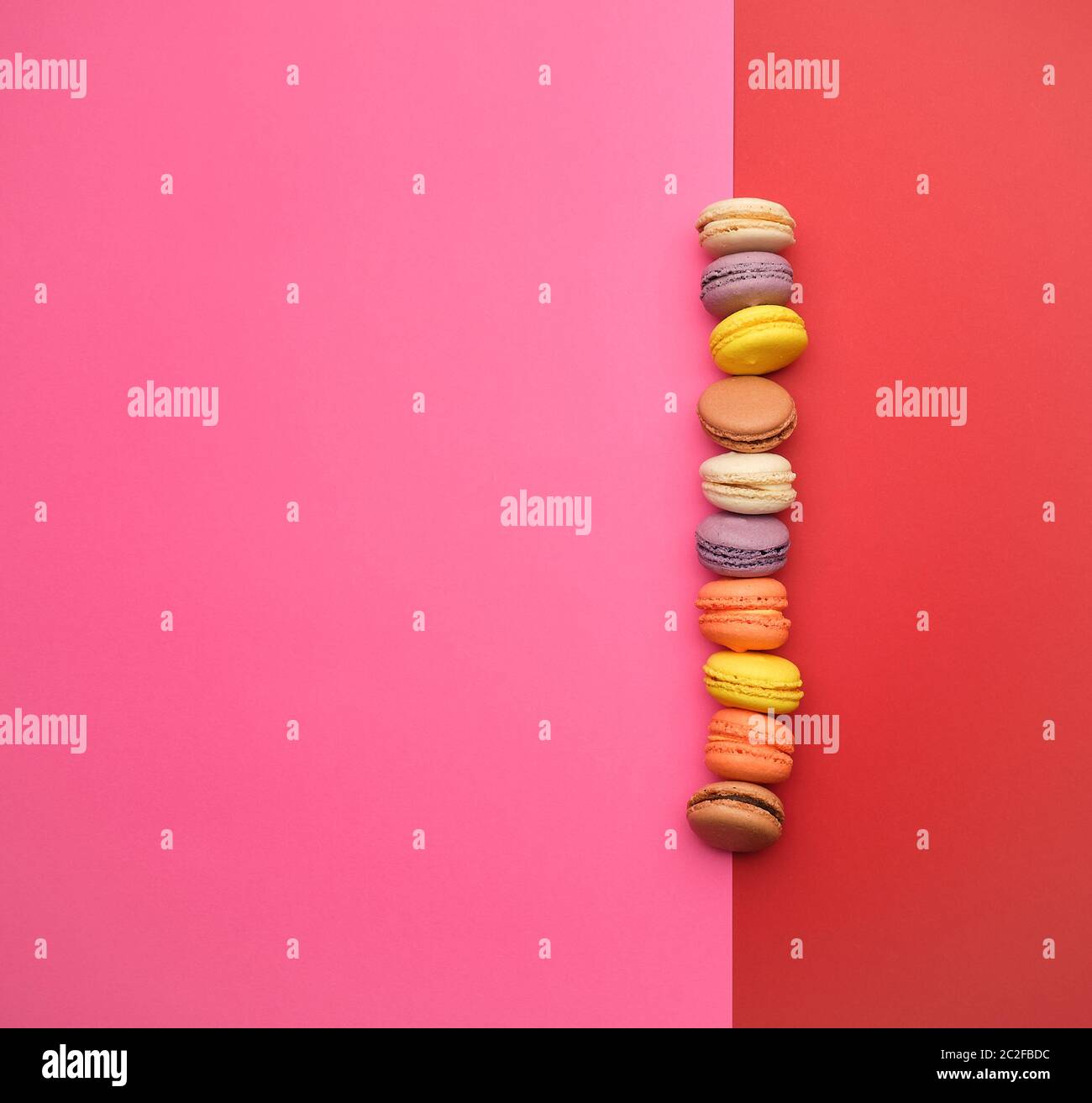round multi-colored baked macarons with cream lie in a line on a pink ...