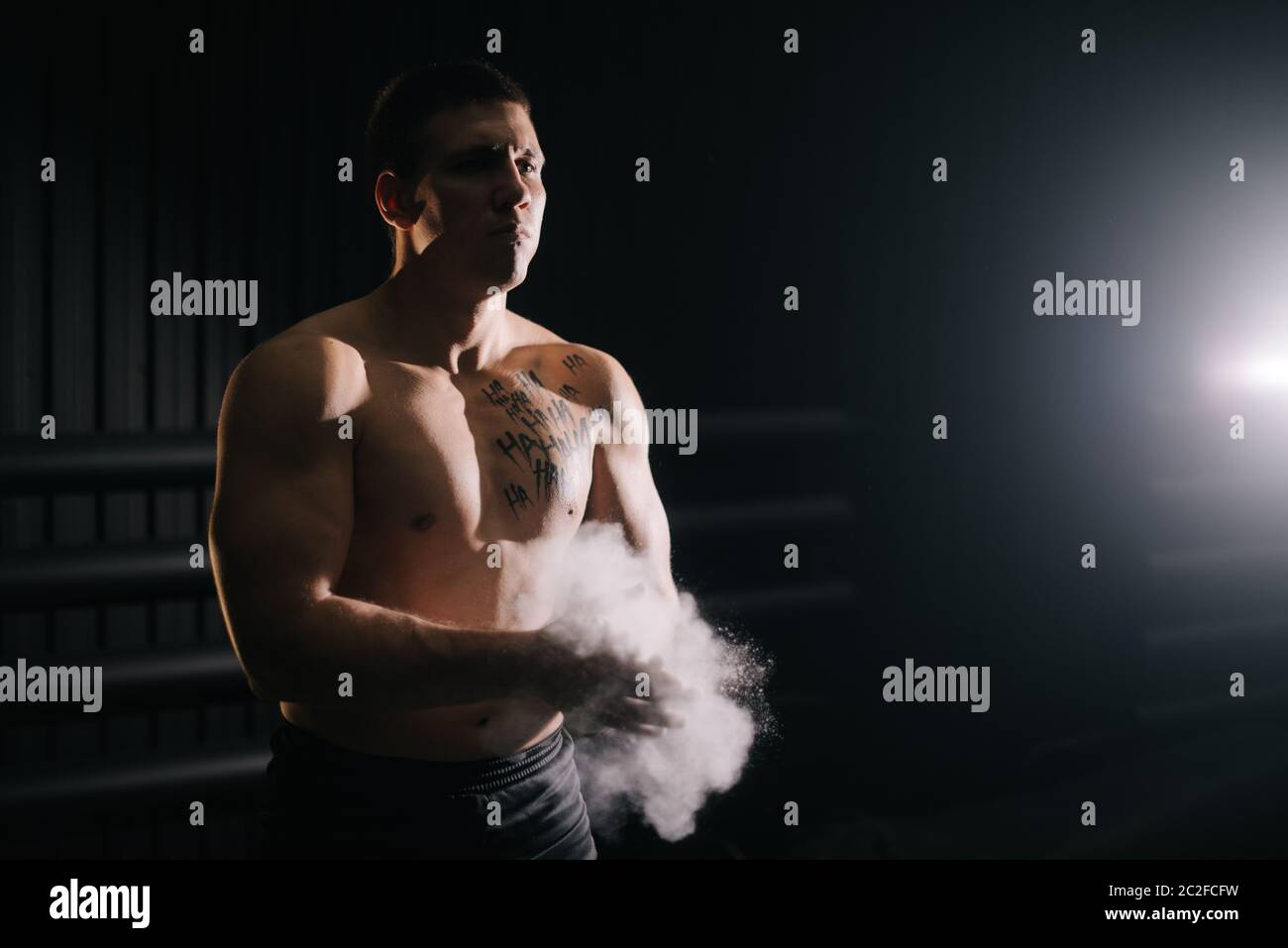 Strong muscular man clapping hands with talc before lifting barbell at ...