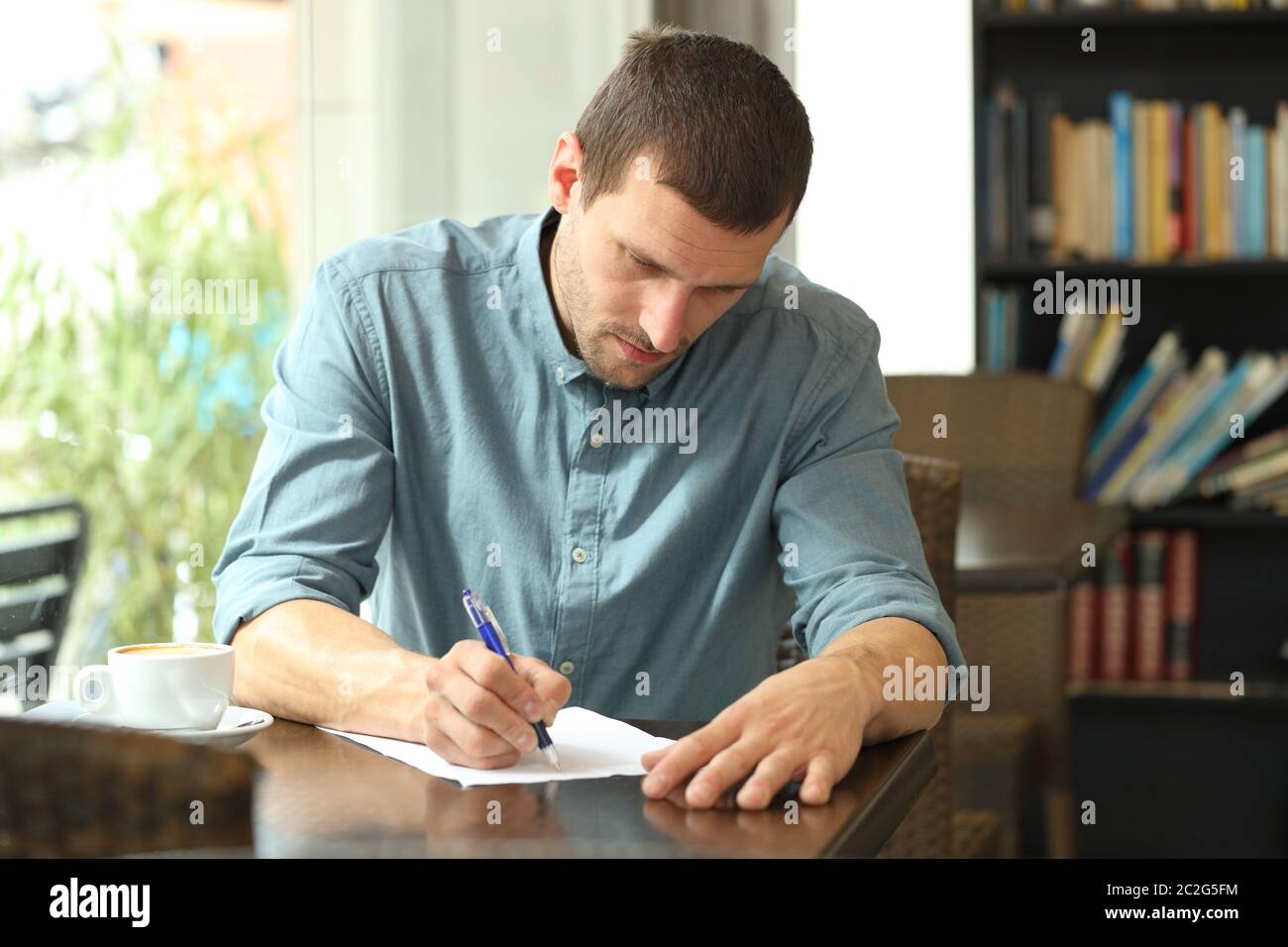 Concentrated man writing notes in a paper sheet using a pen sitting in ...