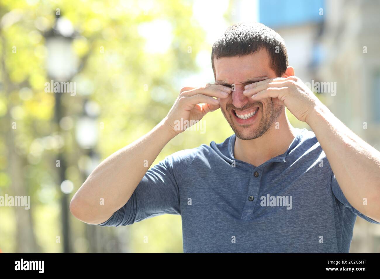 Adult man scratching itchy eyes with both hands standing in the street ...