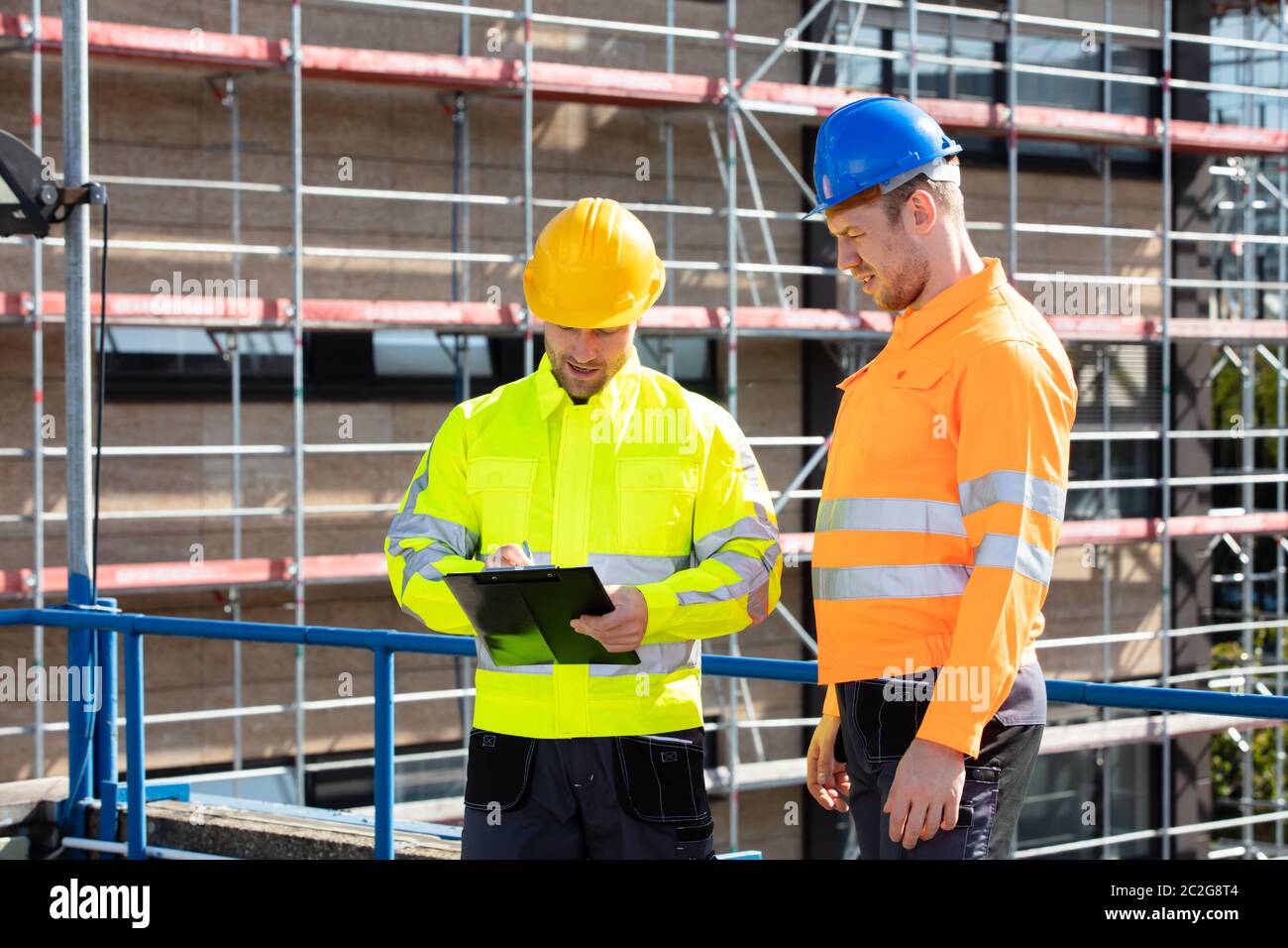 A Male Supervisor Looking At Architect Writing On Clipboard Standing At ...