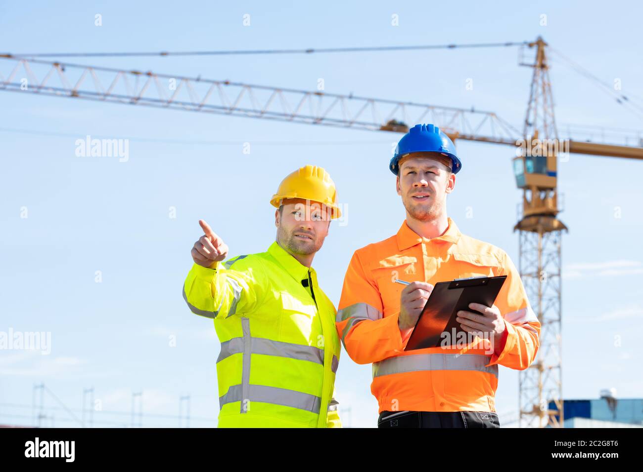Two Young Male Engineers Standing In Front Of Mechanical Crane Working ...