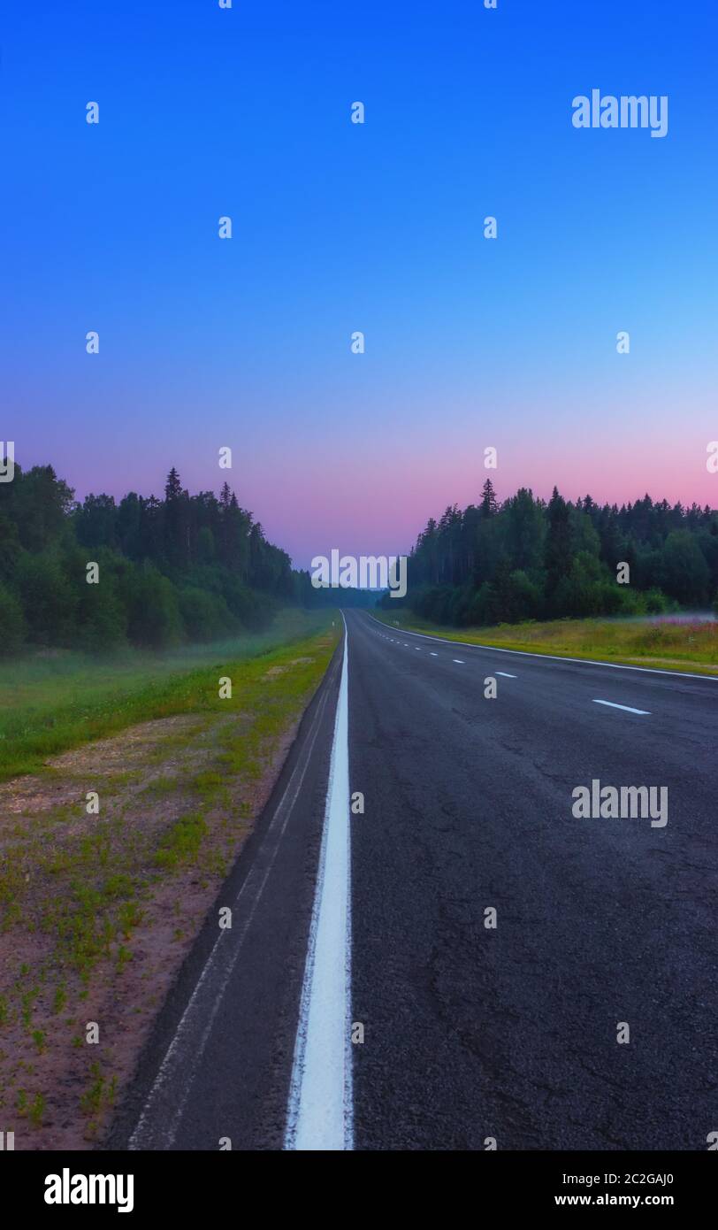 An empty straight asphalt road leads to a pink dawn under the cloudless ...