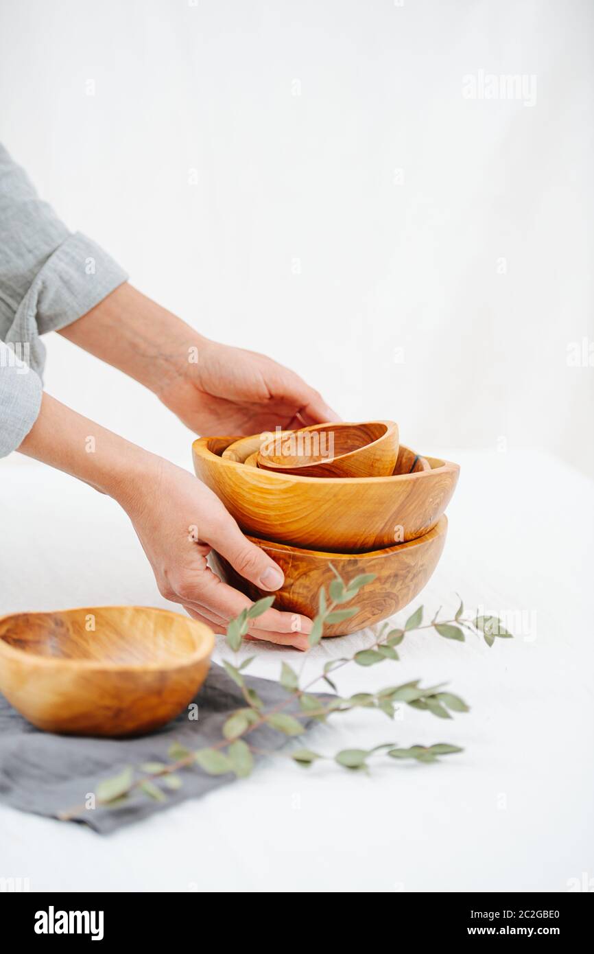 Woman hands placing stack of handmade wooden bowls on a white surface ...