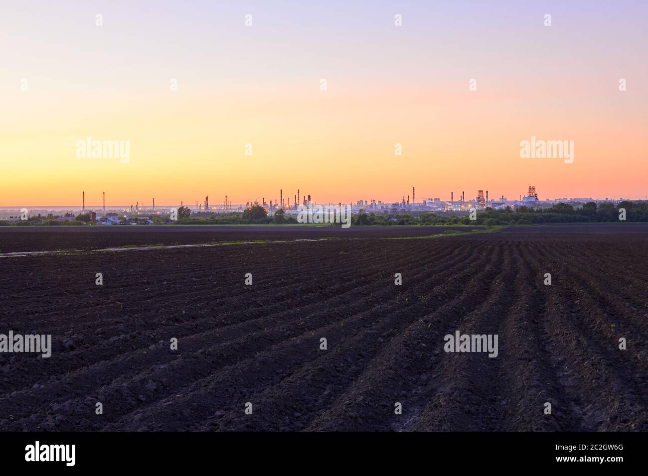 evening rural landscape with plowed fields and a huge oil refinery on ...