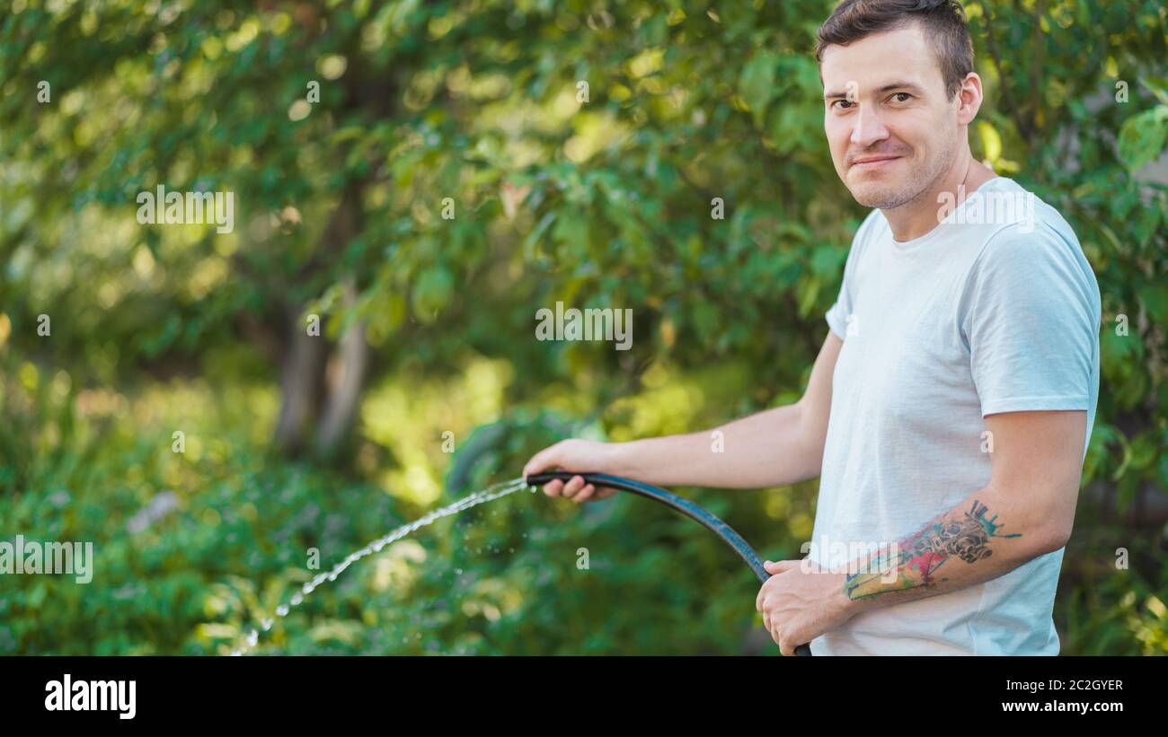 Man watering the garden from hose. Male spraying water on vegetables ...