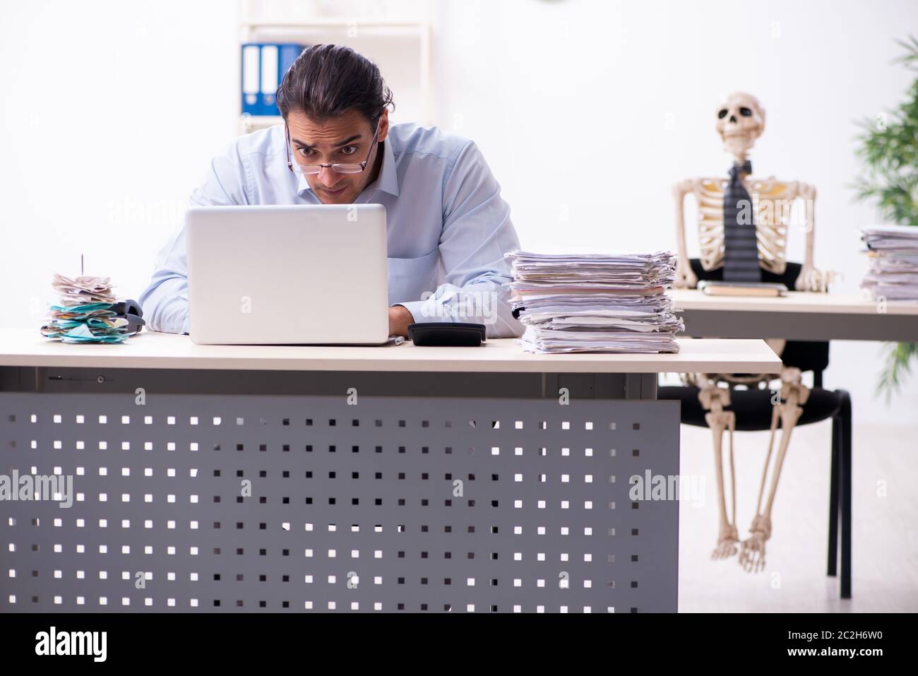 Young employee and skeleton in the office Stock Photo - Alamy