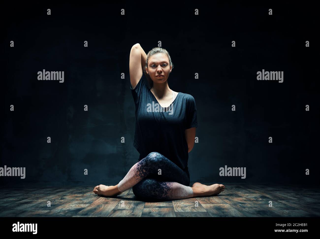 Young woman practicing yoga doing Gomukhasana, cow face pose, in dark ...