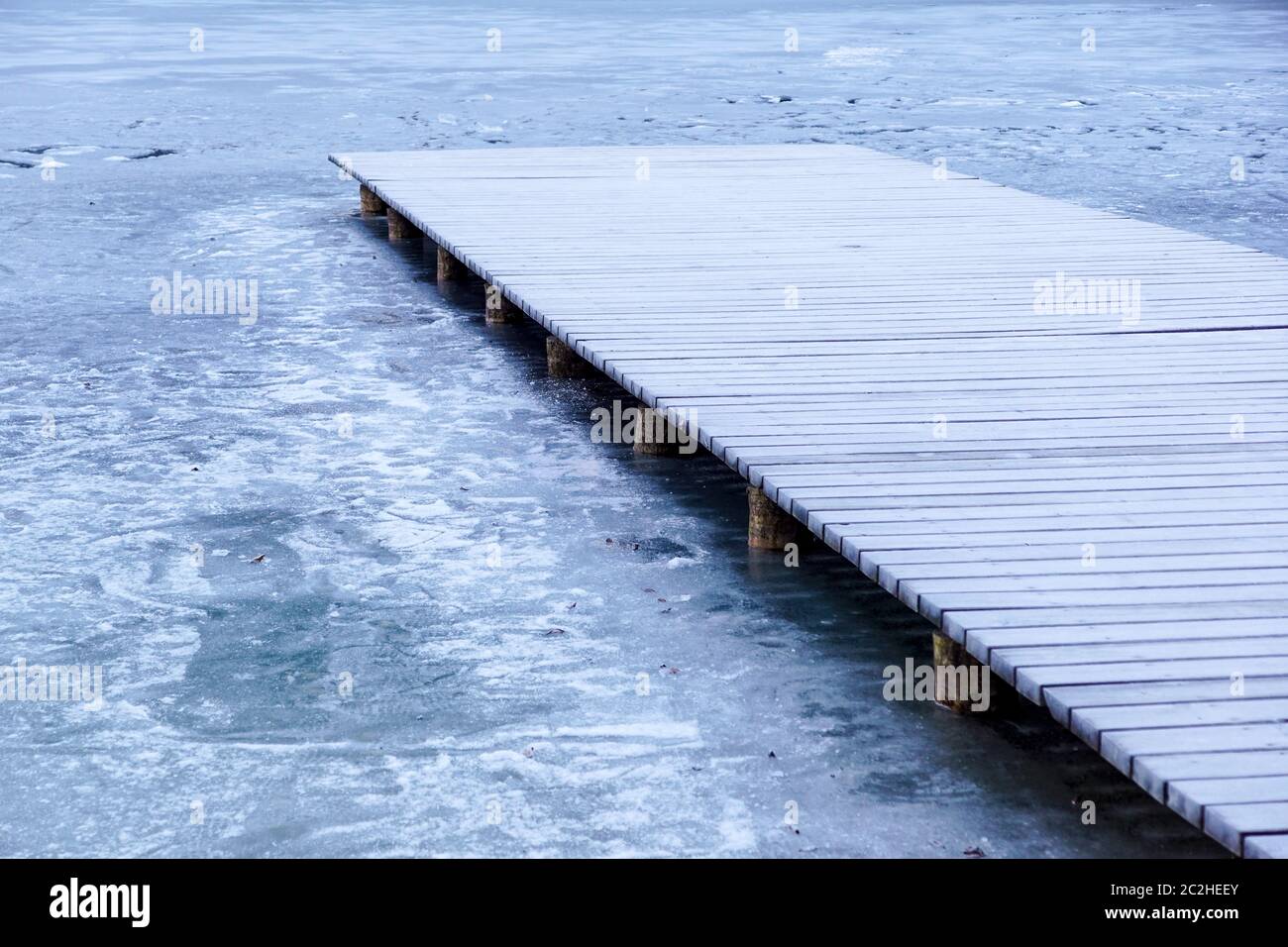Mole pier on the lake. Wooden bridge in forest in winter time with blue ...