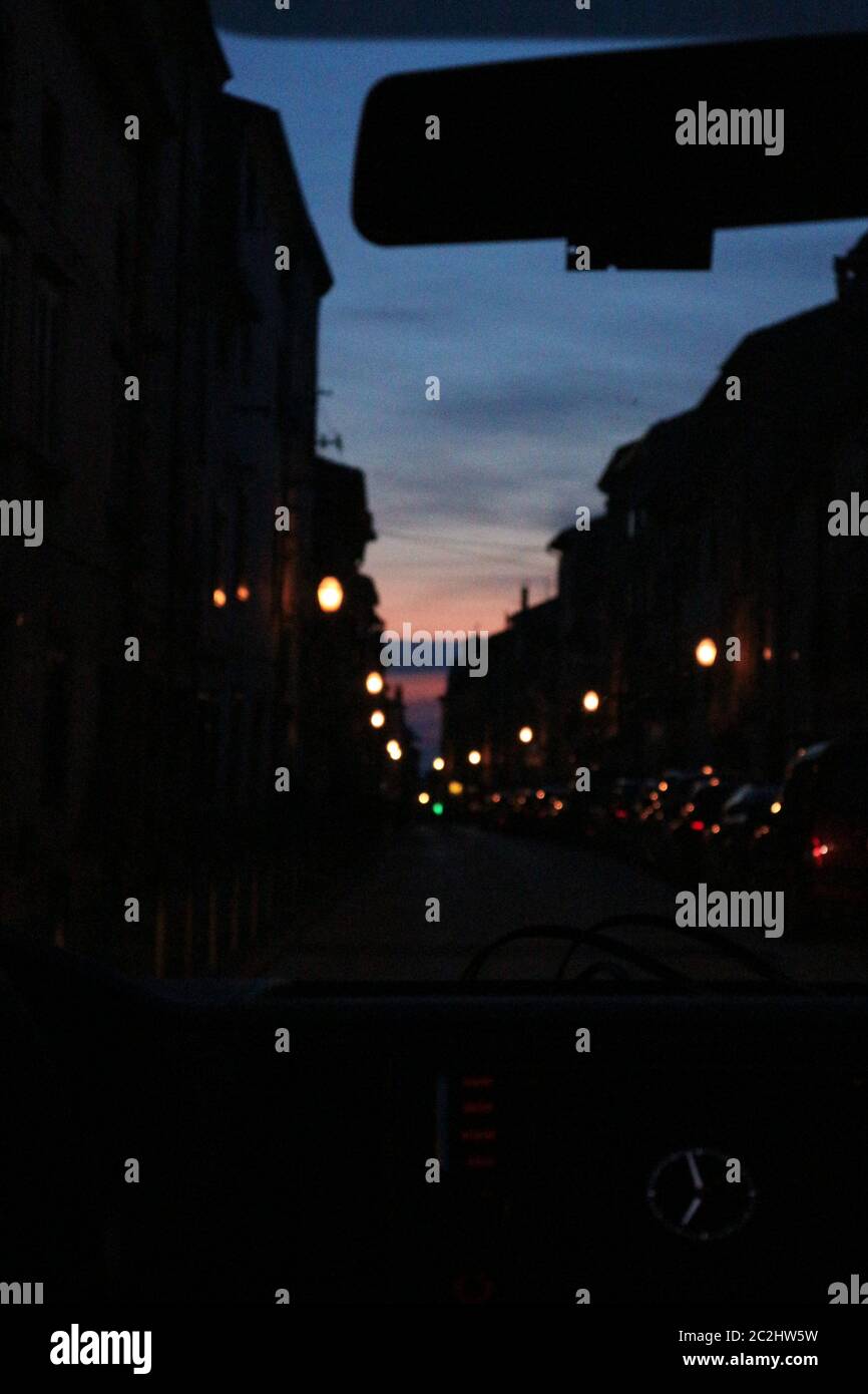 A sunset and blurred street lights photographed out of a car's front ...