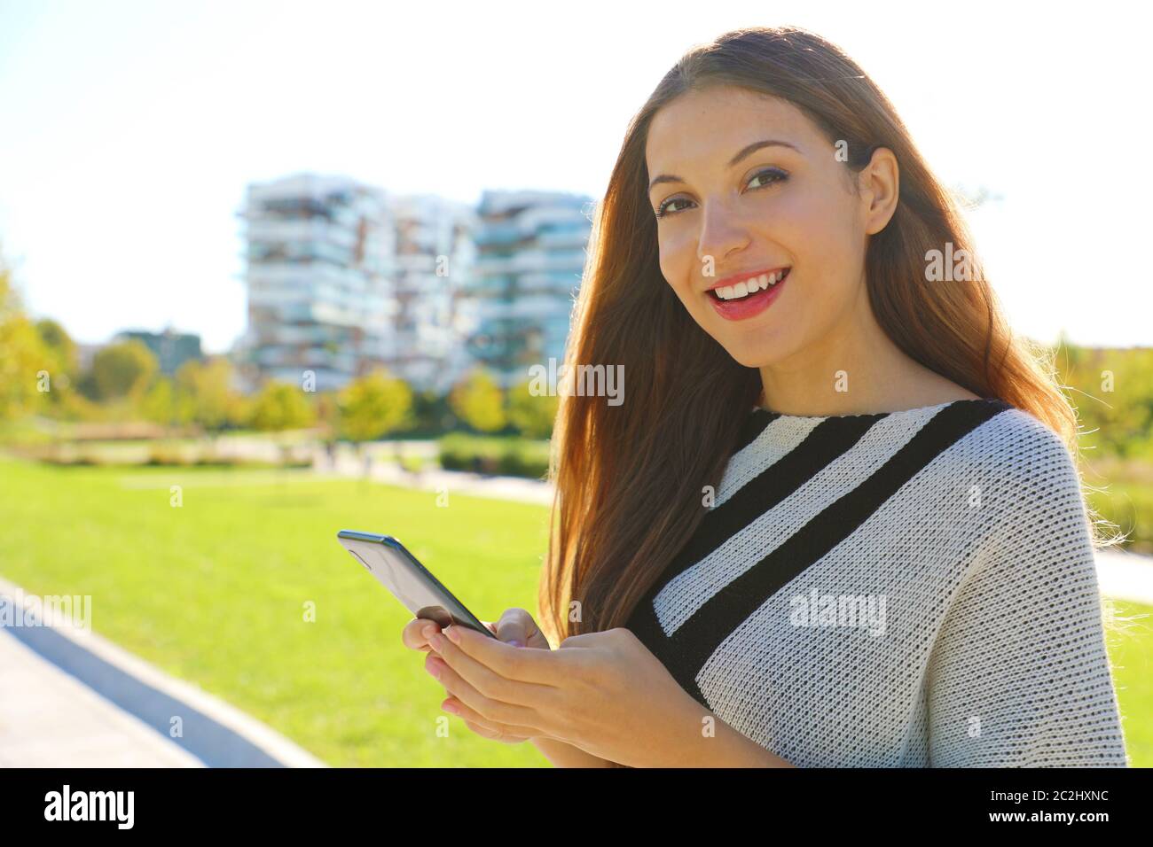 Happy beautiful girl using smart phone in modern city park. Fashion ...