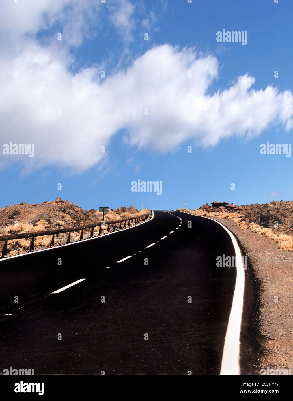 two lane empty road curving to the horizon in a rugged desert landscape ...