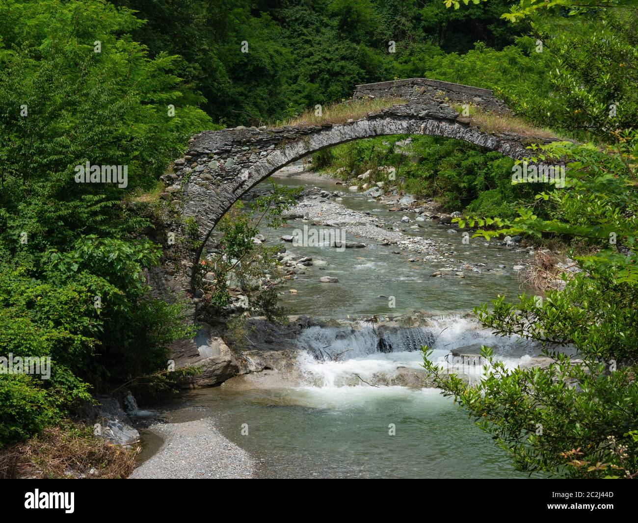 old stone bridge in ruins, over a stream surrounded by trees Stock ...