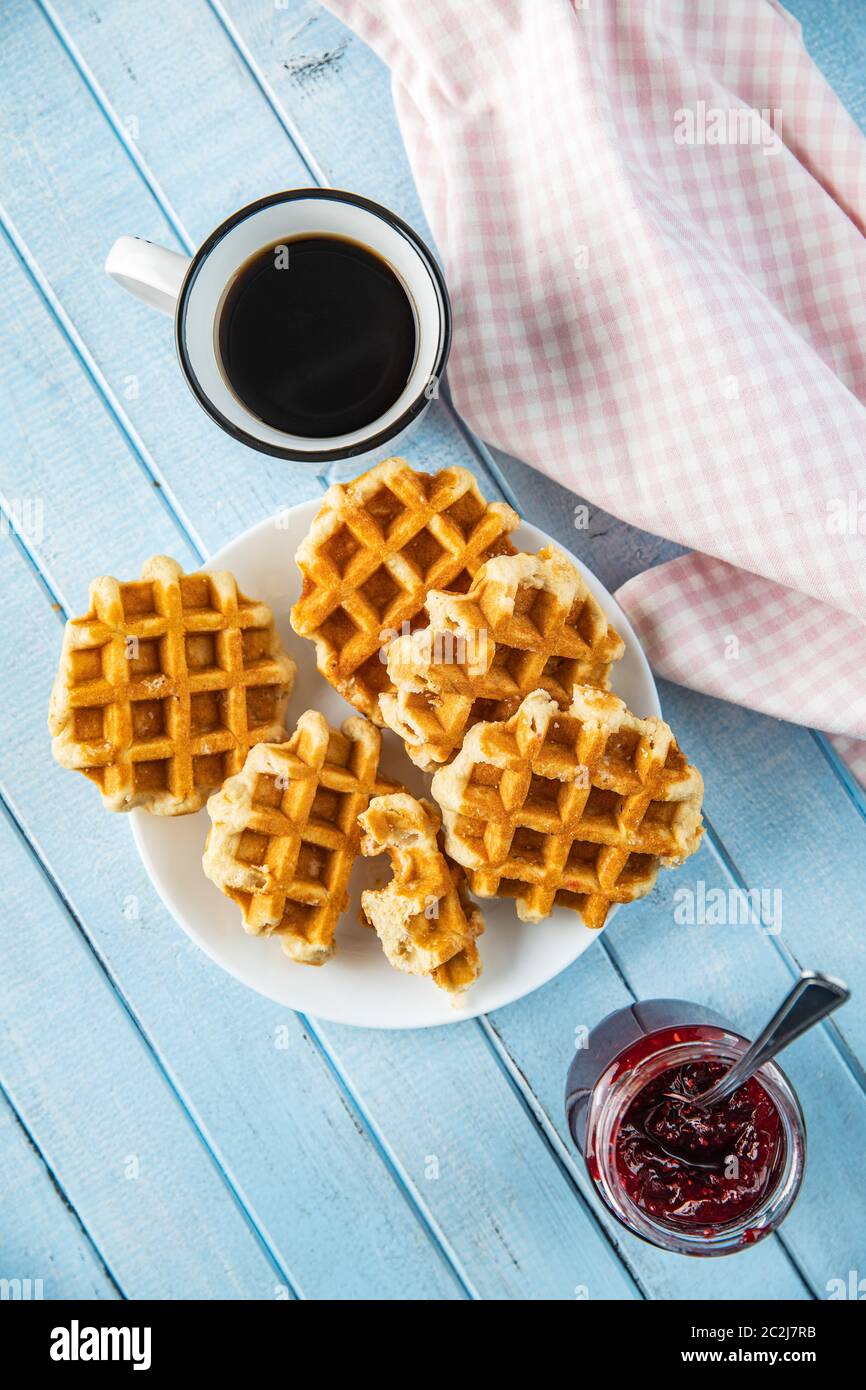 Tasty sweet waffles with raspberry jam and tea cup on blue table. Top ...