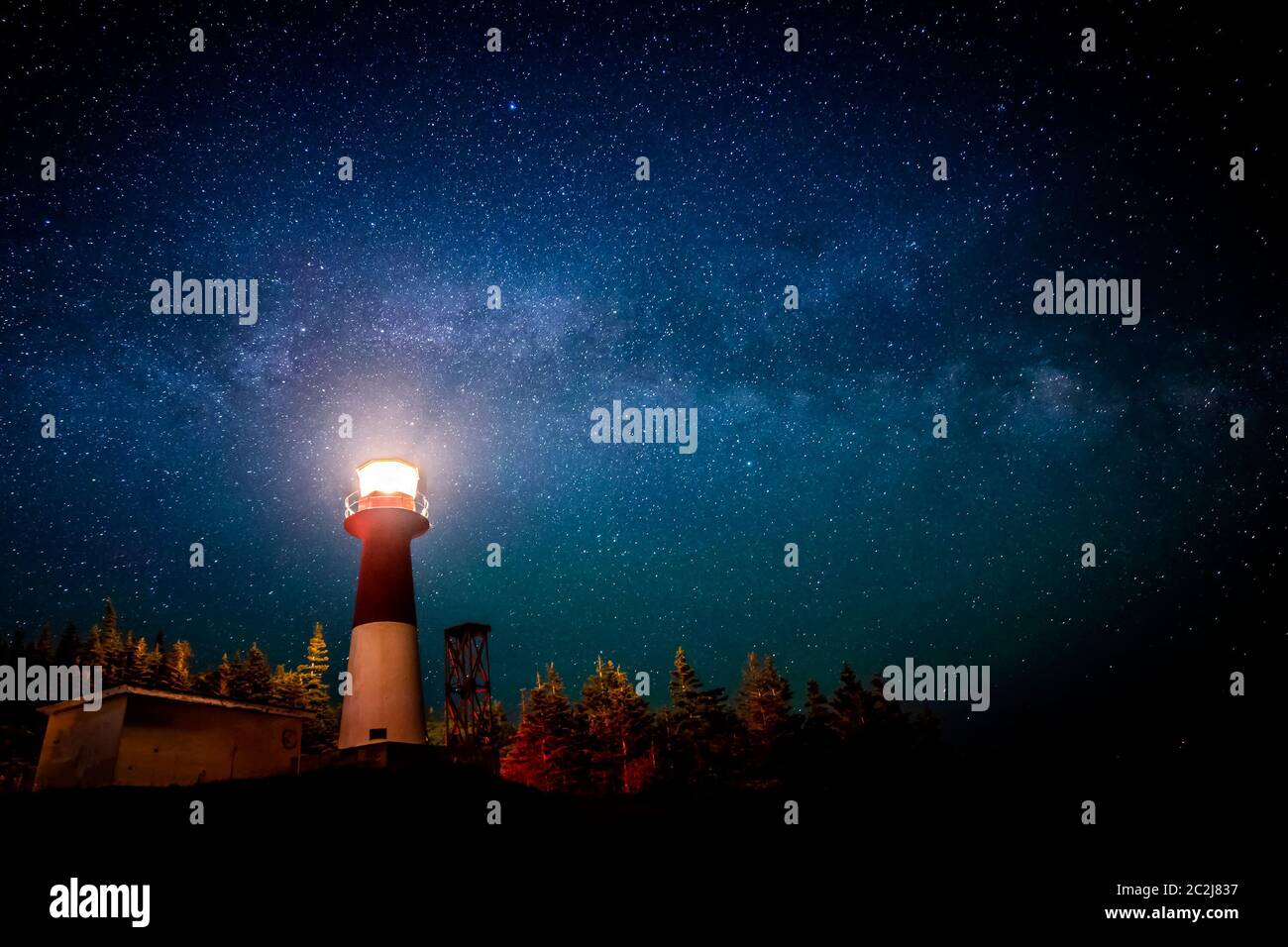 A lighthouse at night with a star filled sky above. The light in the ...
