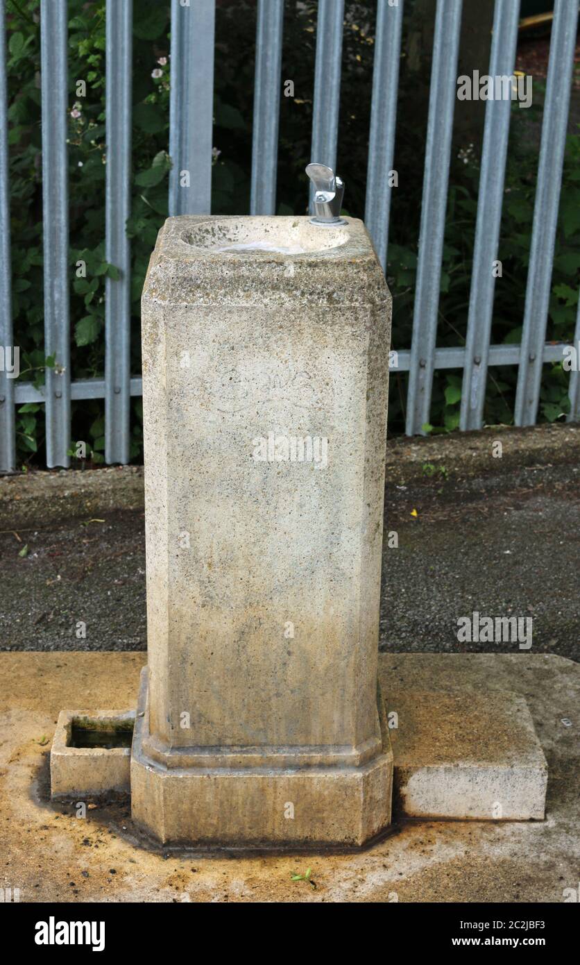 Concrete drinking fountain on a plinth in a park with a grey metal ...