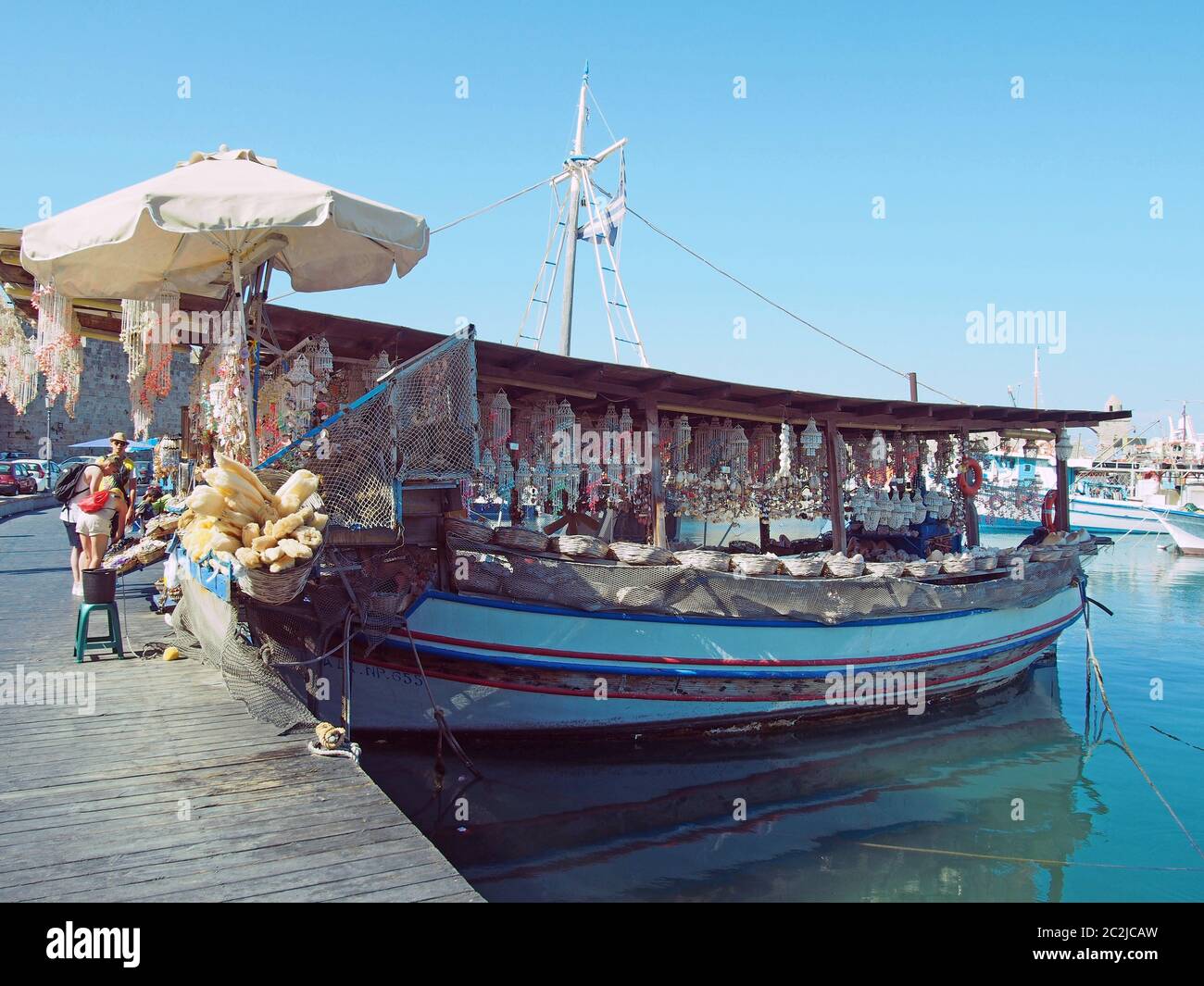 tourists look a shells and sponges for sale on a boat in the harbour in ...