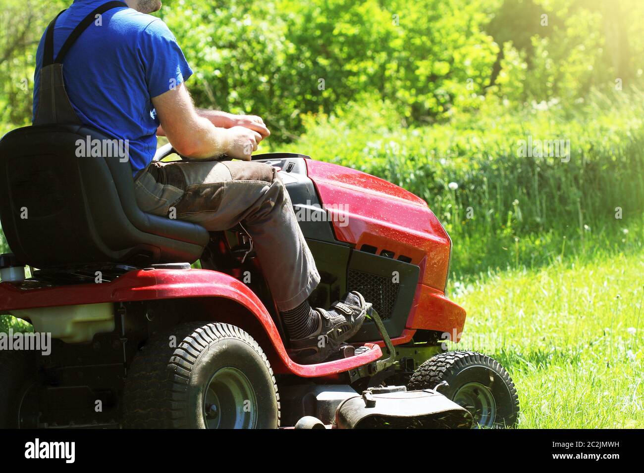 Gardener driving a riding lawn mower in a garden Stock Photo - Alamy