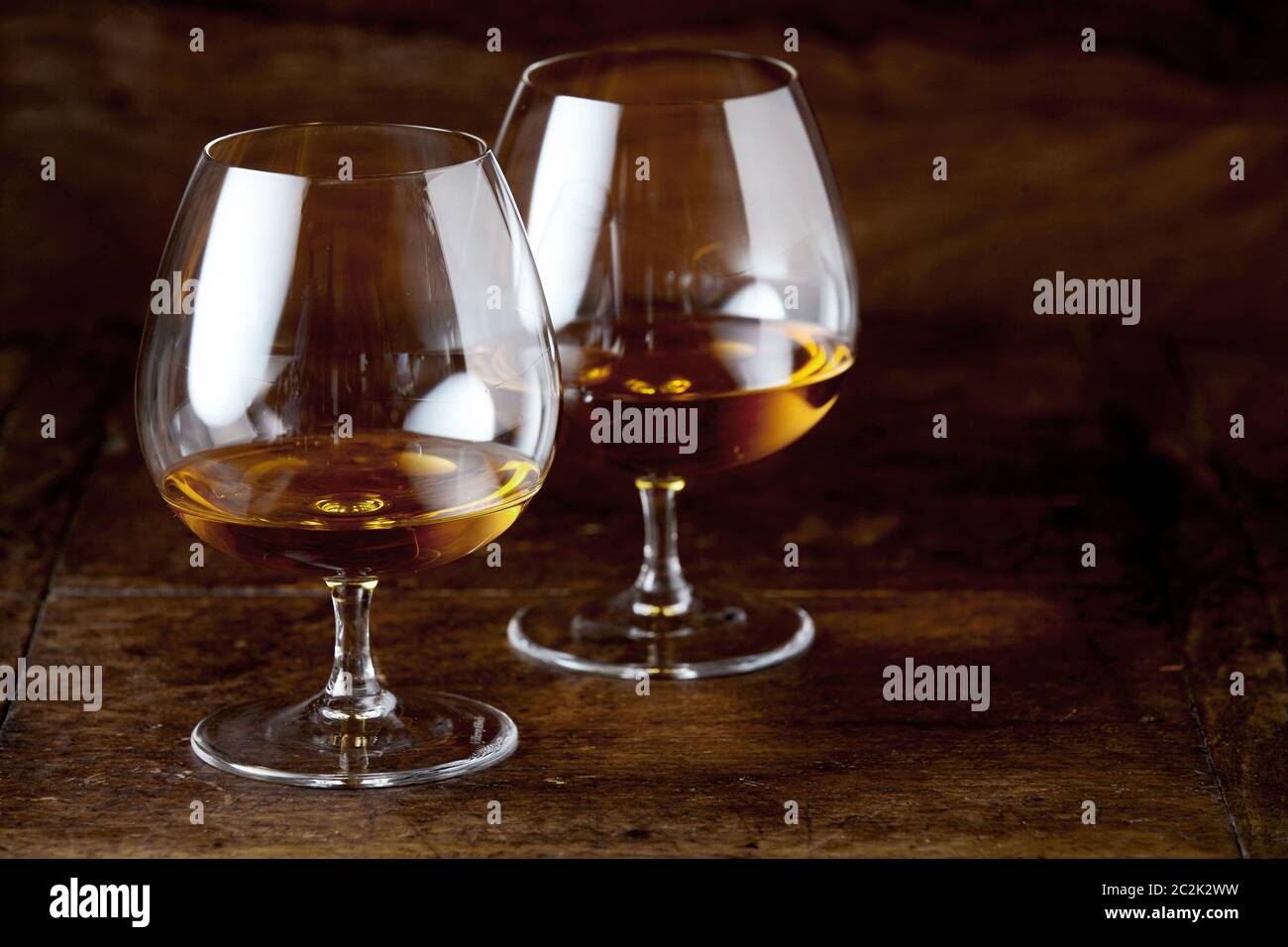 Two brandy snifter glasses with cognac in close-up on dark brown wooden ...