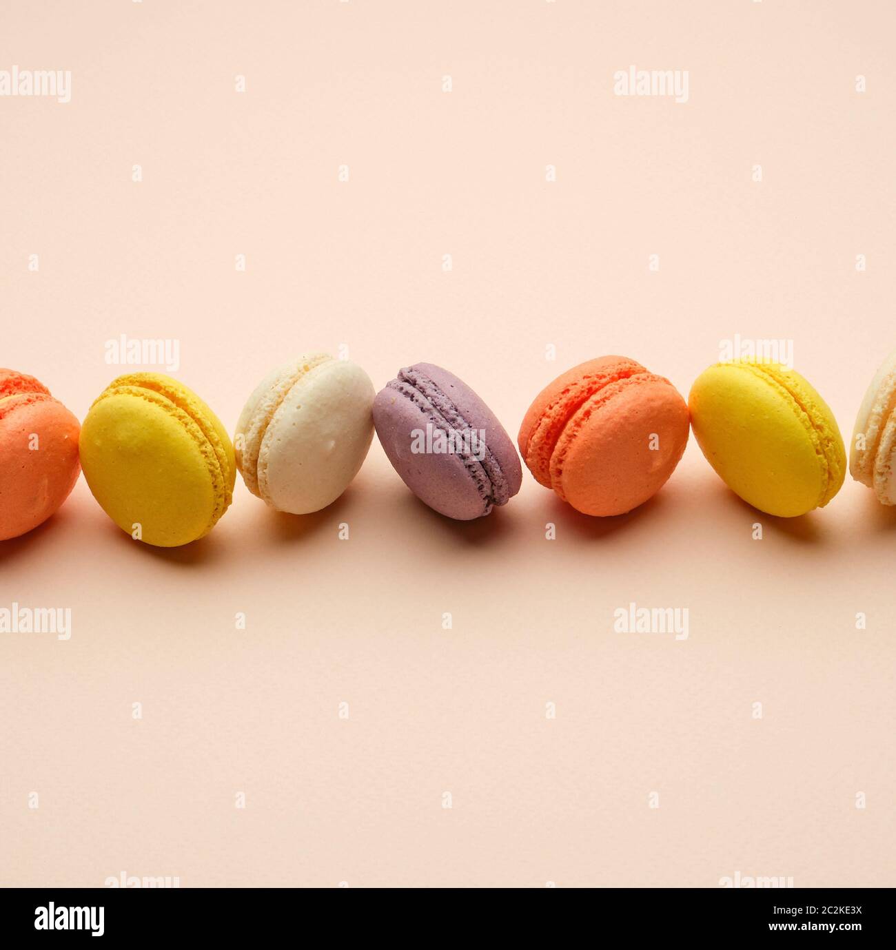 round multi-colored baked macarons with cream lie in a line on a beige ...