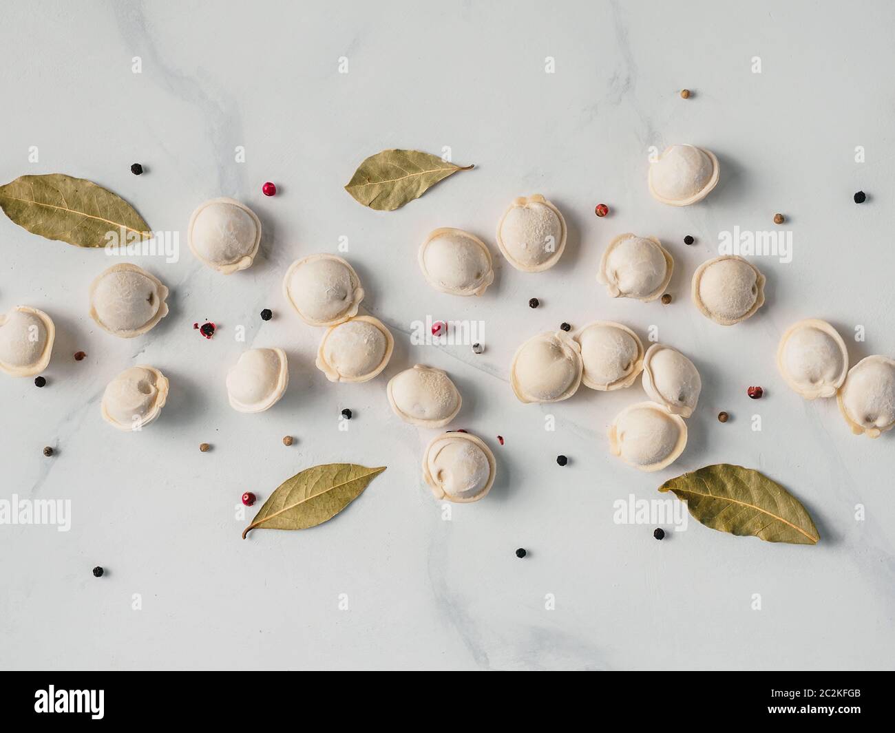 Pattern of frozen uncooked russian pelmeni with peppercorns and bay ...