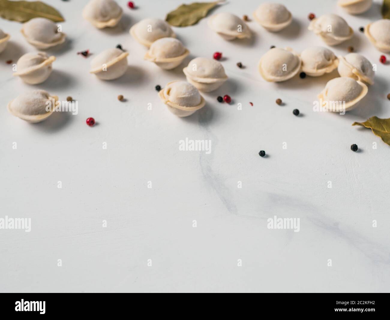 Pattern of frozen uncooked russian pelmeni with peppercorns and bay ...